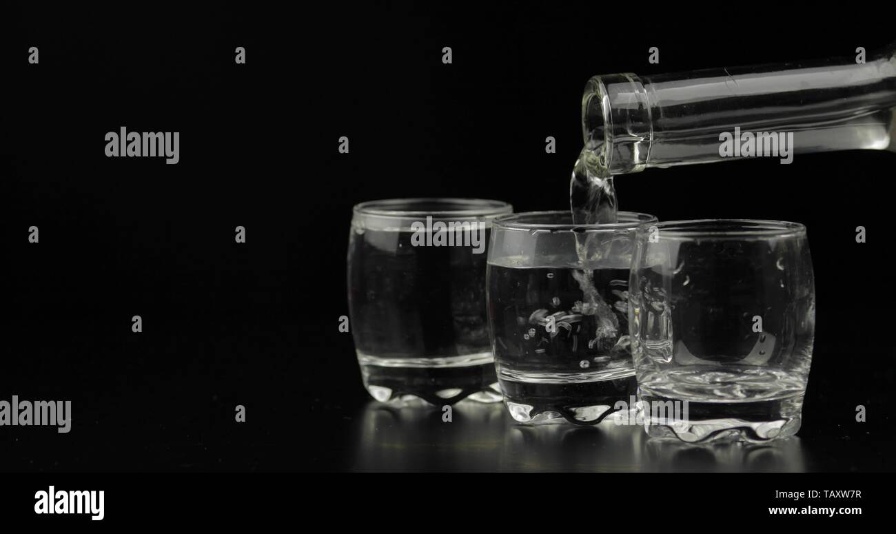 Pouring up shots of vodka from a bottle into glass against black ...