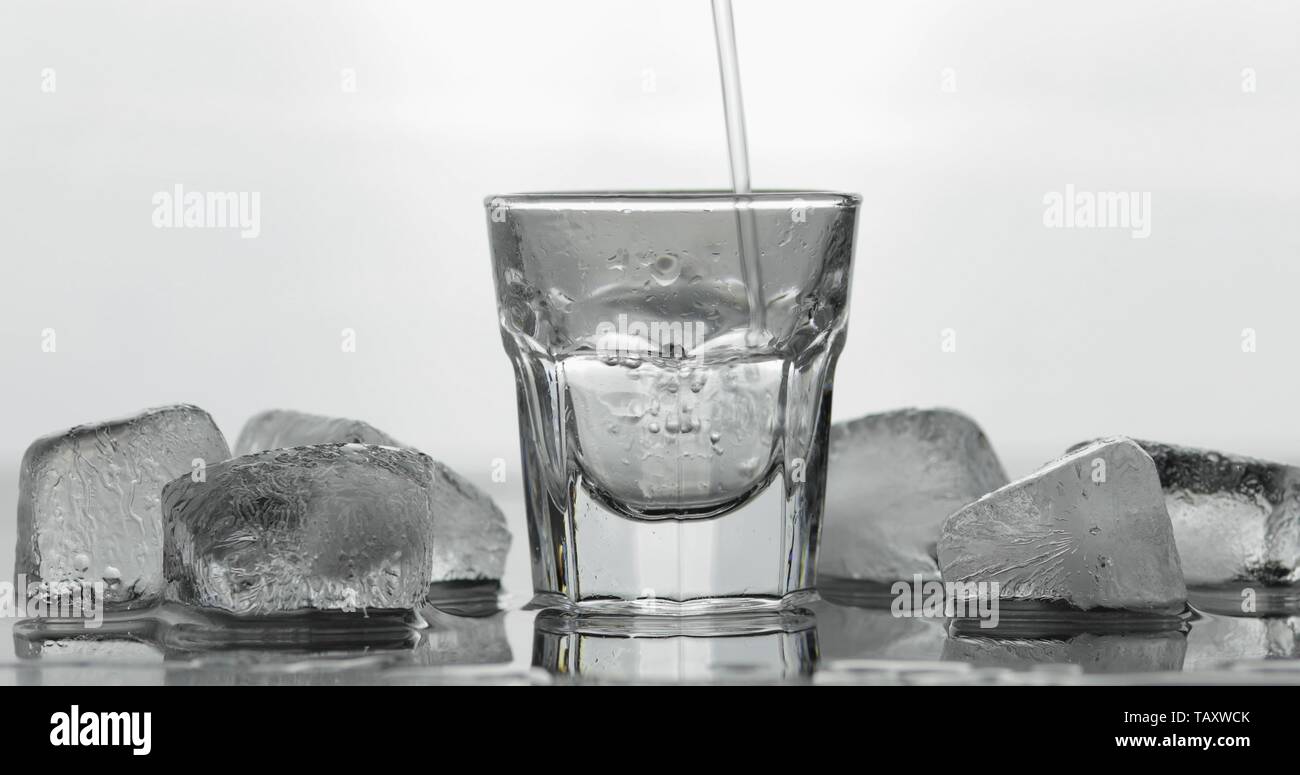 Pouring up shot of vodka into glass with ice against black background ...