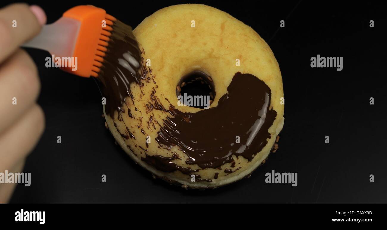 Delicious melted chocolate syrup spreading over a donut on black ...