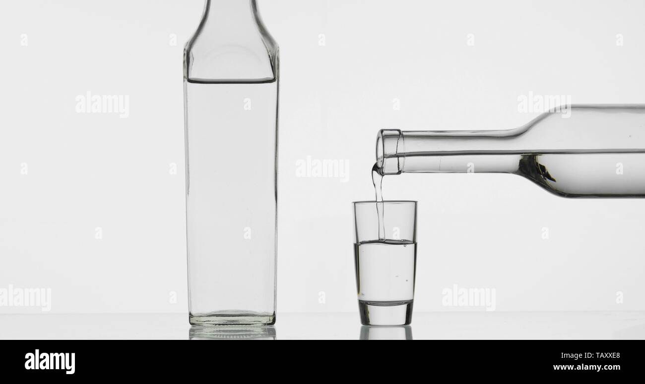 Pouring up shot of vodka from a bottle into glass against white ...