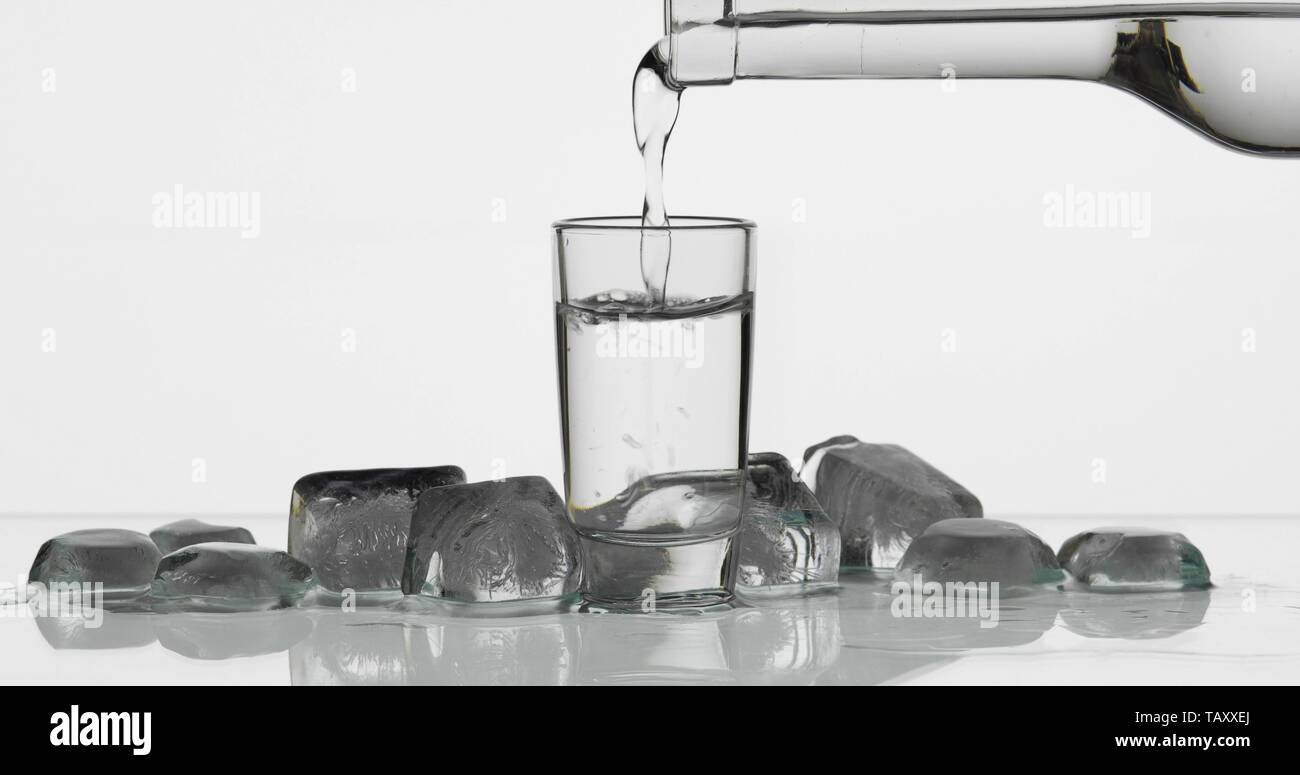 Pouring up shot of vodka from a bottle into glass against white ...