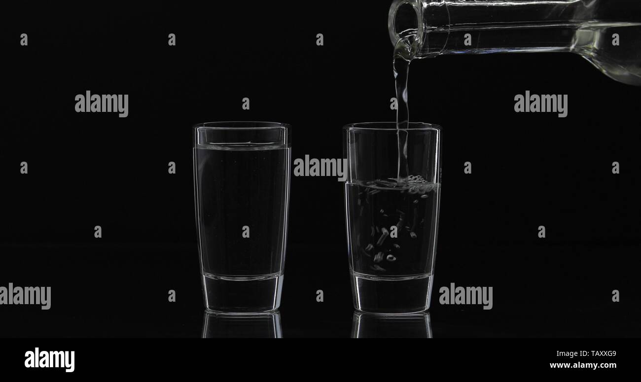 Pouring up shot of vodka from a bottle into glass against black ...