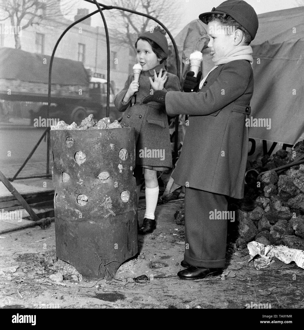 Children warming themselves round the watchman's fire. 5th January 1956 ...