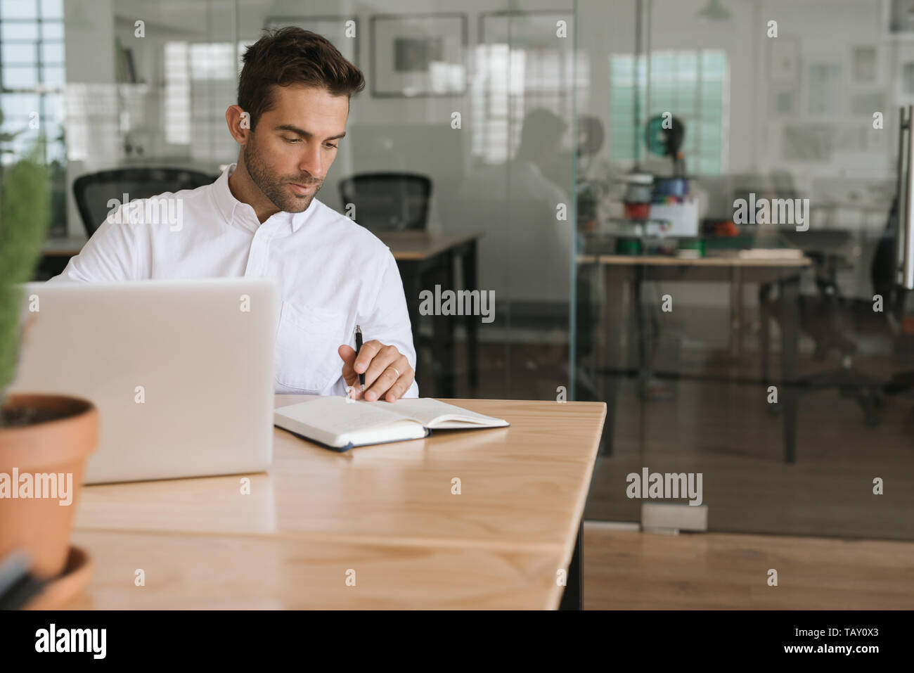 Focused young businessman working online with a laptop and writing down ...
