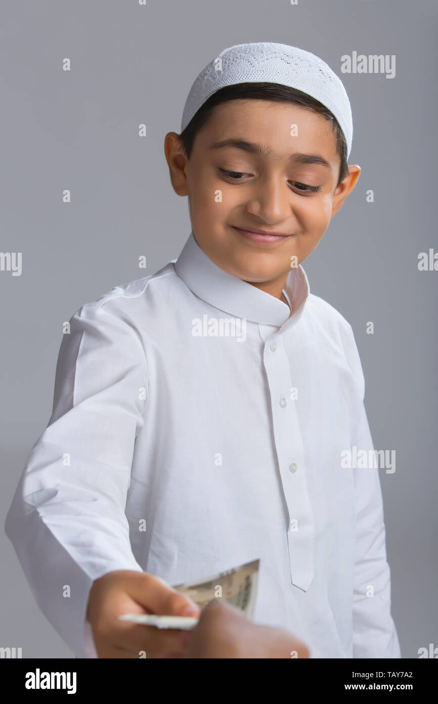 Young Muslim boy wearing cap smiling and giving away money Stock Photo ...