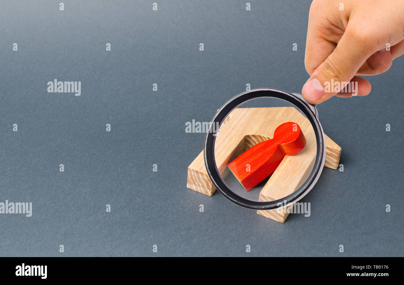 Magnifying glass is looking at a red figurine of a man and a fallen ...