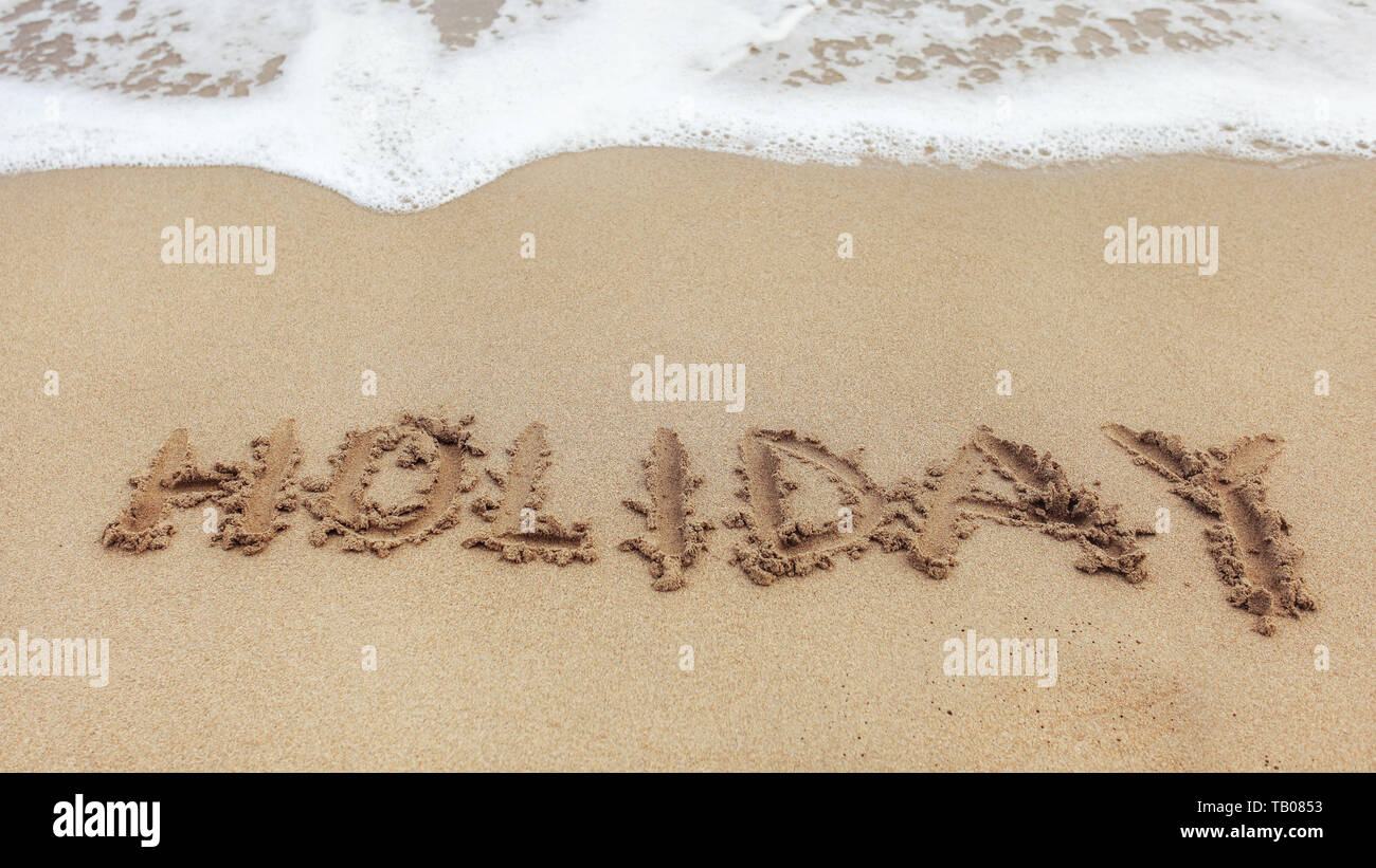 Word HOLIDAY written on wet sand of beach, small spot of white sea ...