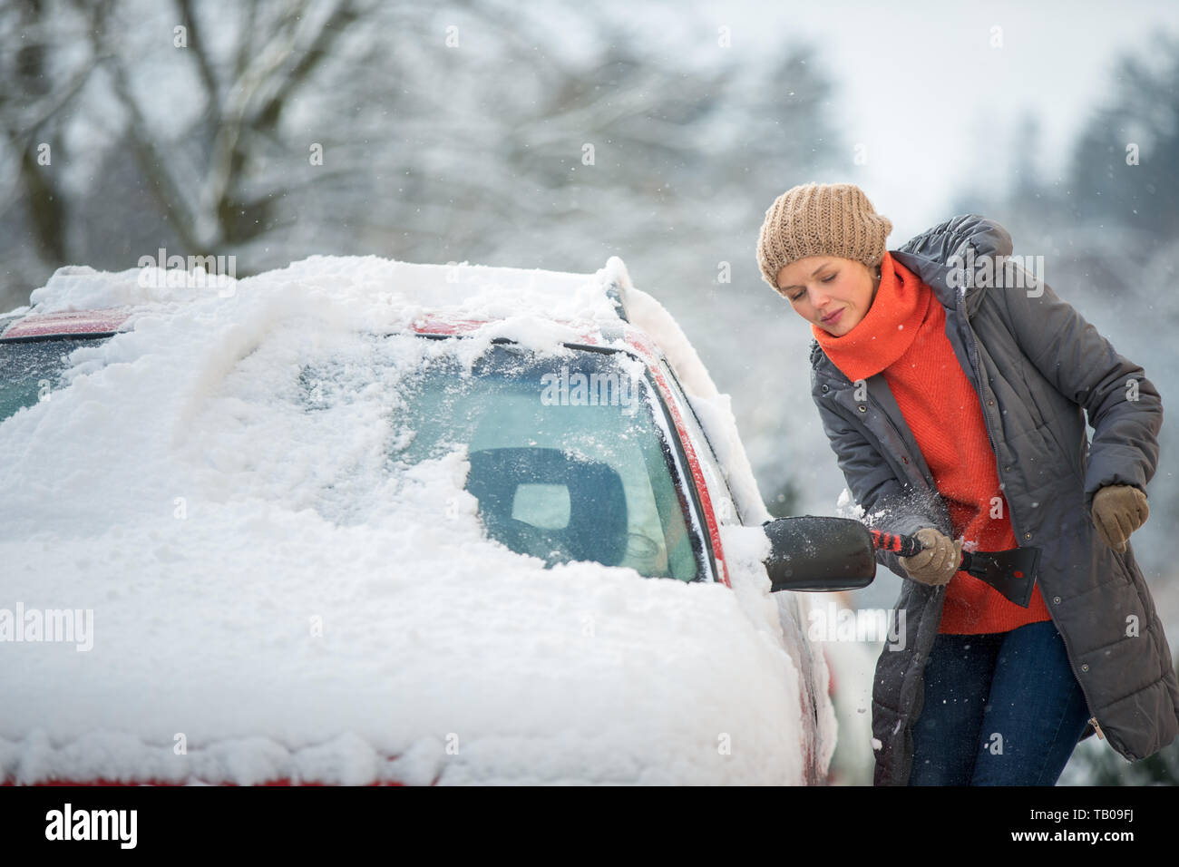 Pretty, young woman cleaning her car from snow after heavy snowstorm ...