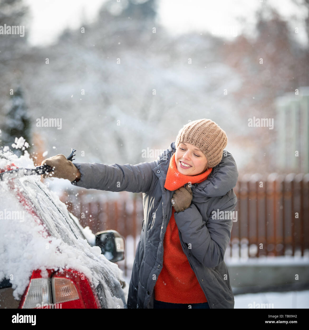 Pretty, young woman cleaning her car from snow after heavy snowstorm ...