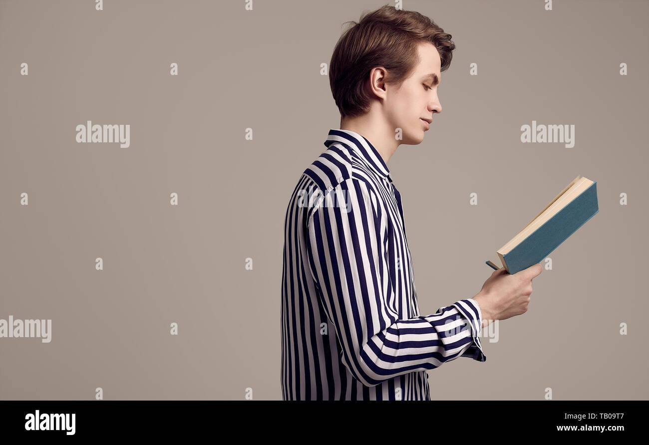 Fashion portrait of young handsome man in striped shirt reading a book ...