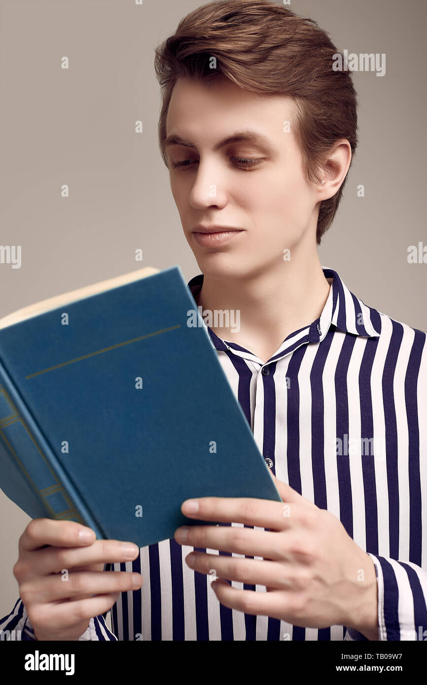 Fashion portrait of young handsome man in striped shirt reading a book ...