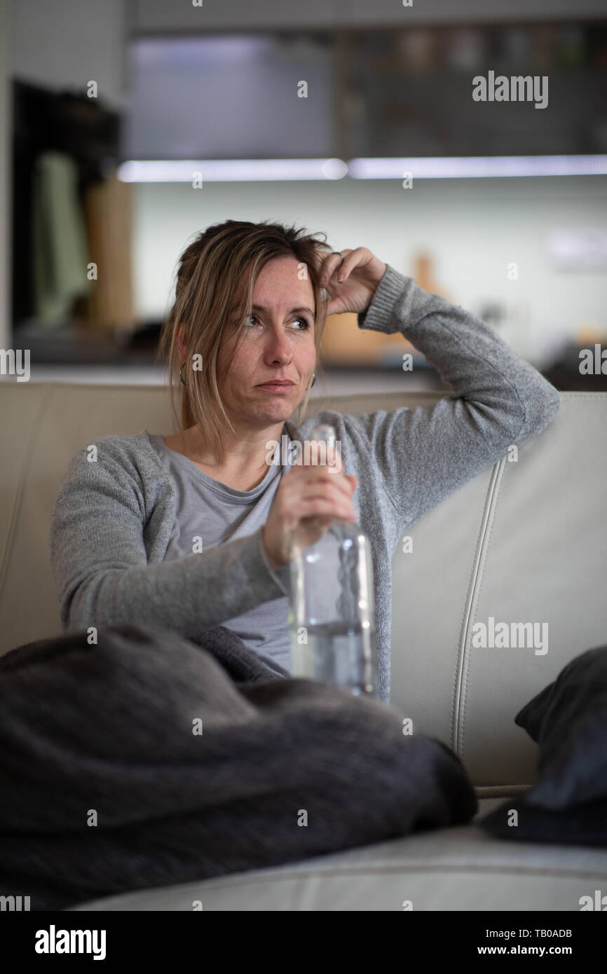 Midlle aged woman at home with a bottle of strong alcohol in her hands ...