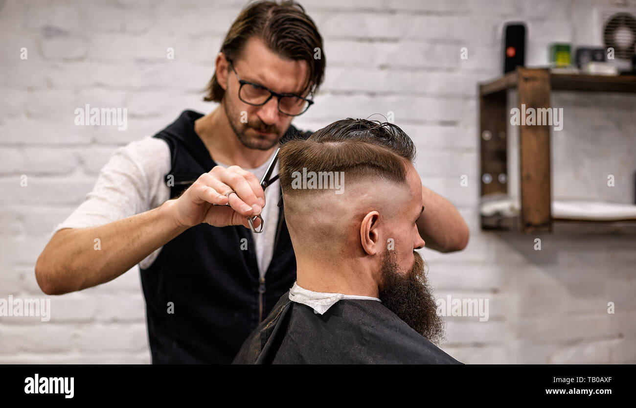 Master cuts hair and beard of men in the barbershop, hairdresser makes ...