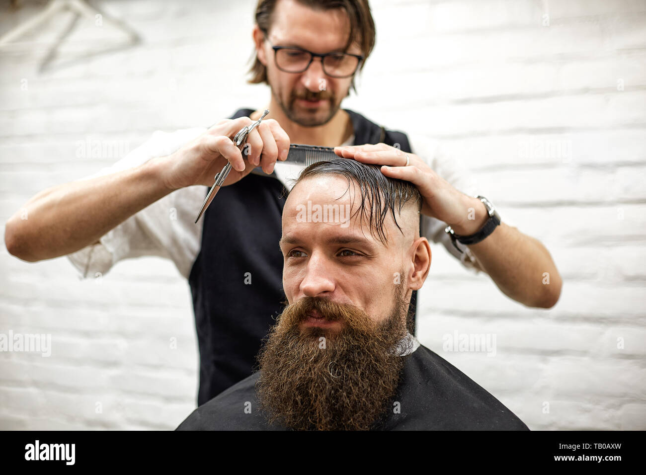 Master cuts hair and beard of men in the barbershop, hairdresser makes ...