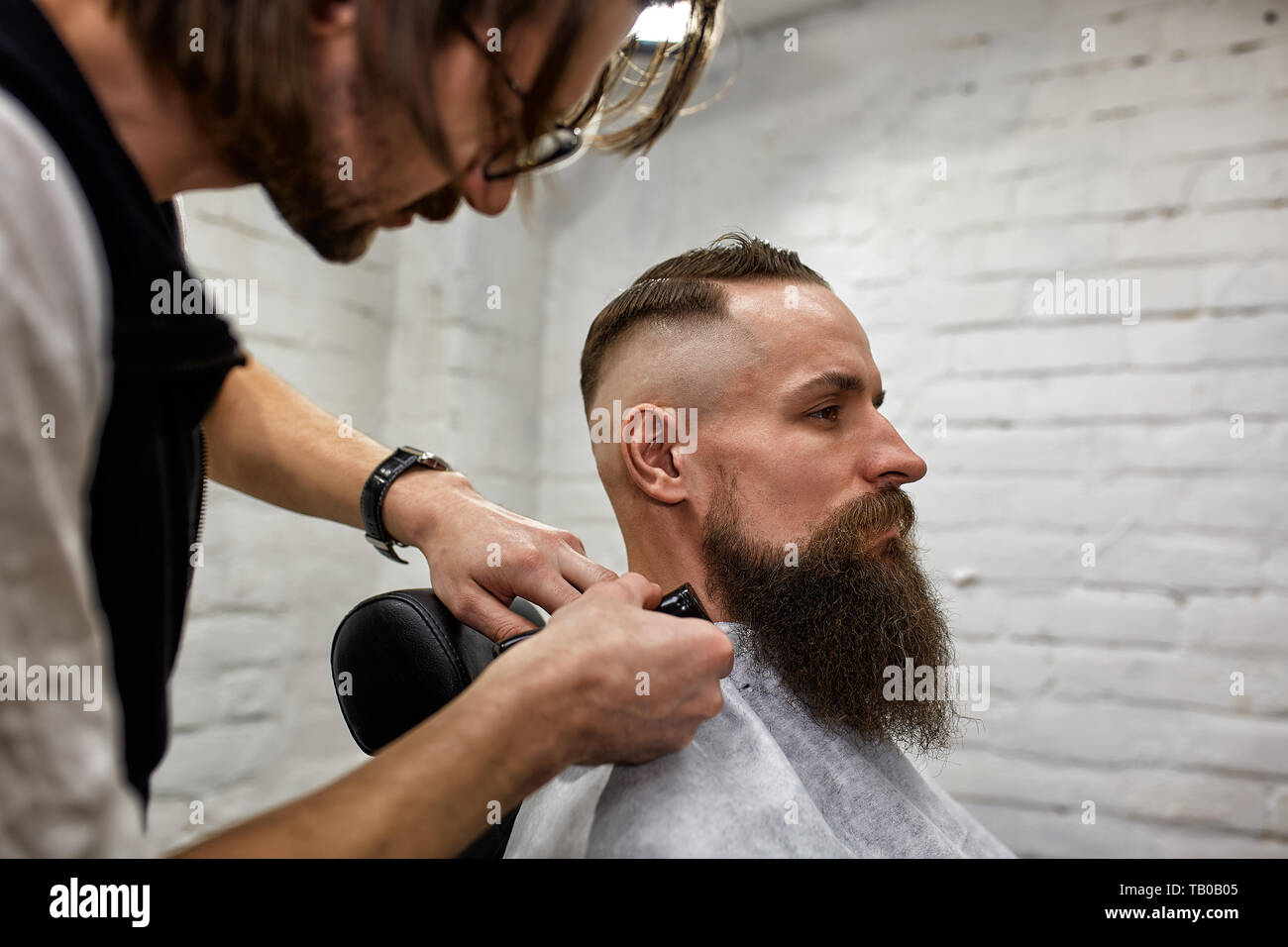 Master cuts hair and beard of men in the barbershop, hairdresser makes ...