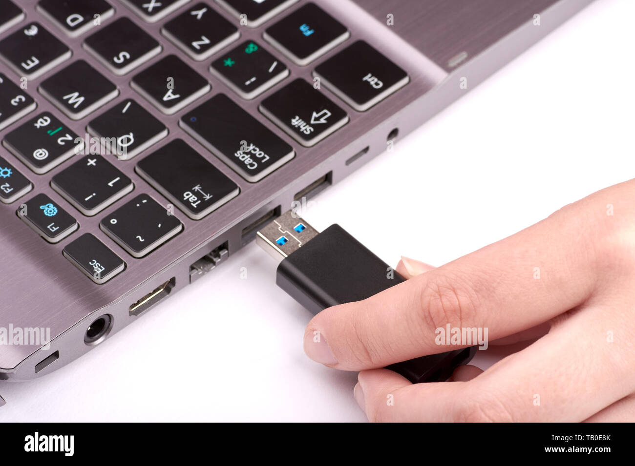 Closeup view of silver laptop. A woman holds a black flash drive or ...