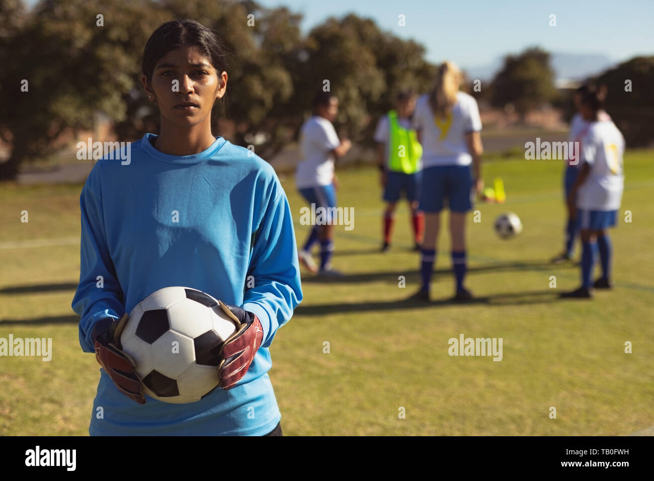 Female soccer player with football standing at sports field Stock Photo ...