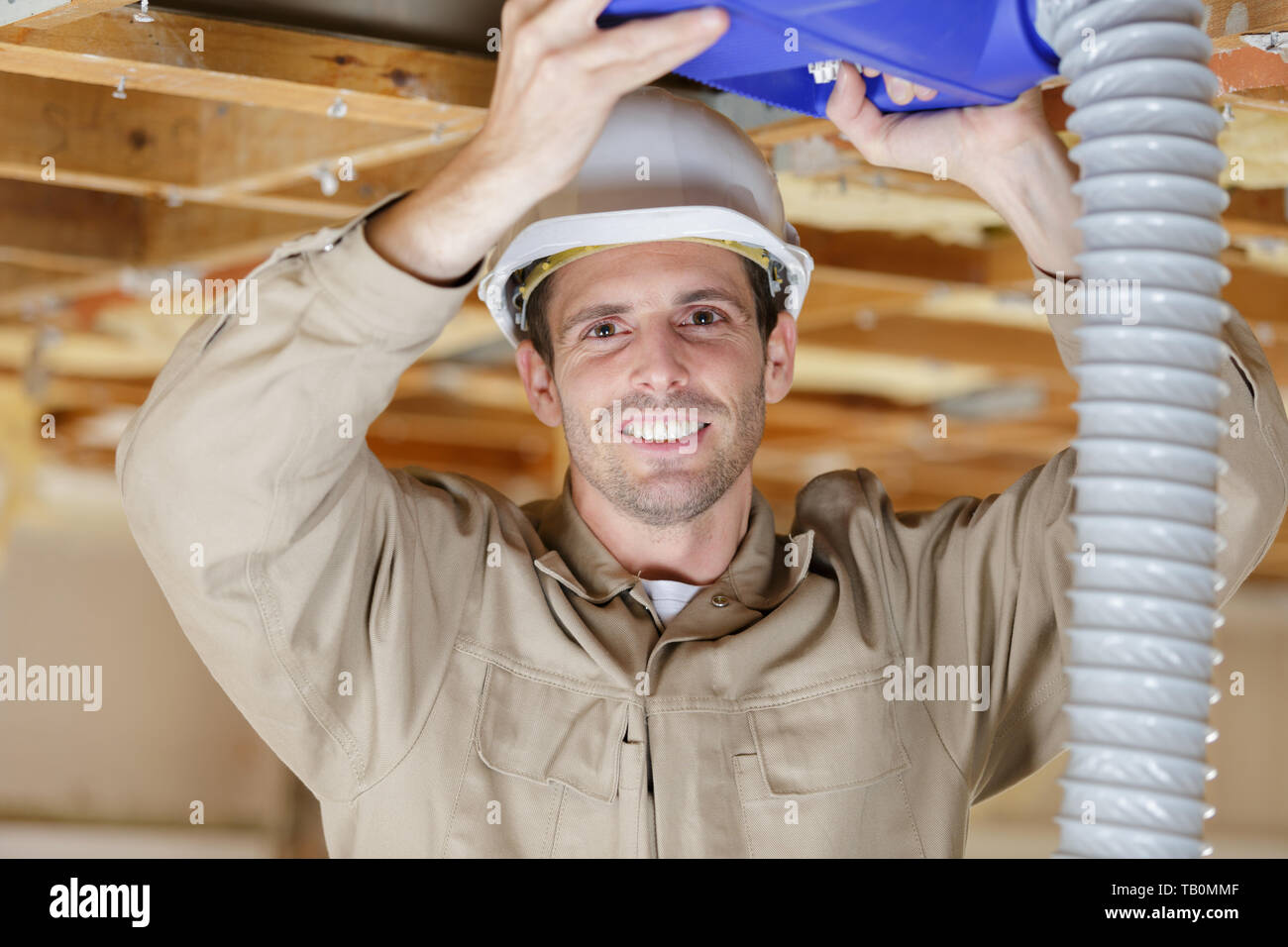 tradesman fitting ventilation system into overhead rafters Stock Photo ...