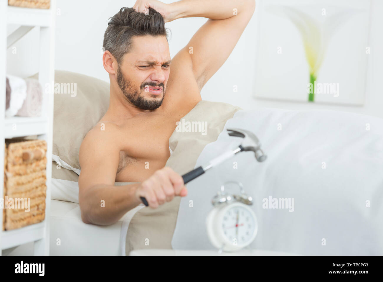 man smashing alarm clock with hammer on bed Stock Photo - Alamy
