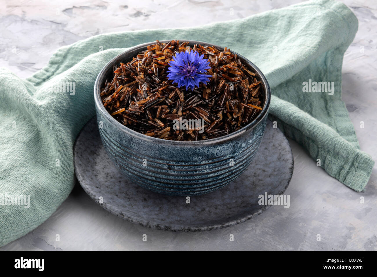 Wild black rice with an edible flower, a blue cornflower, on teal and ...
