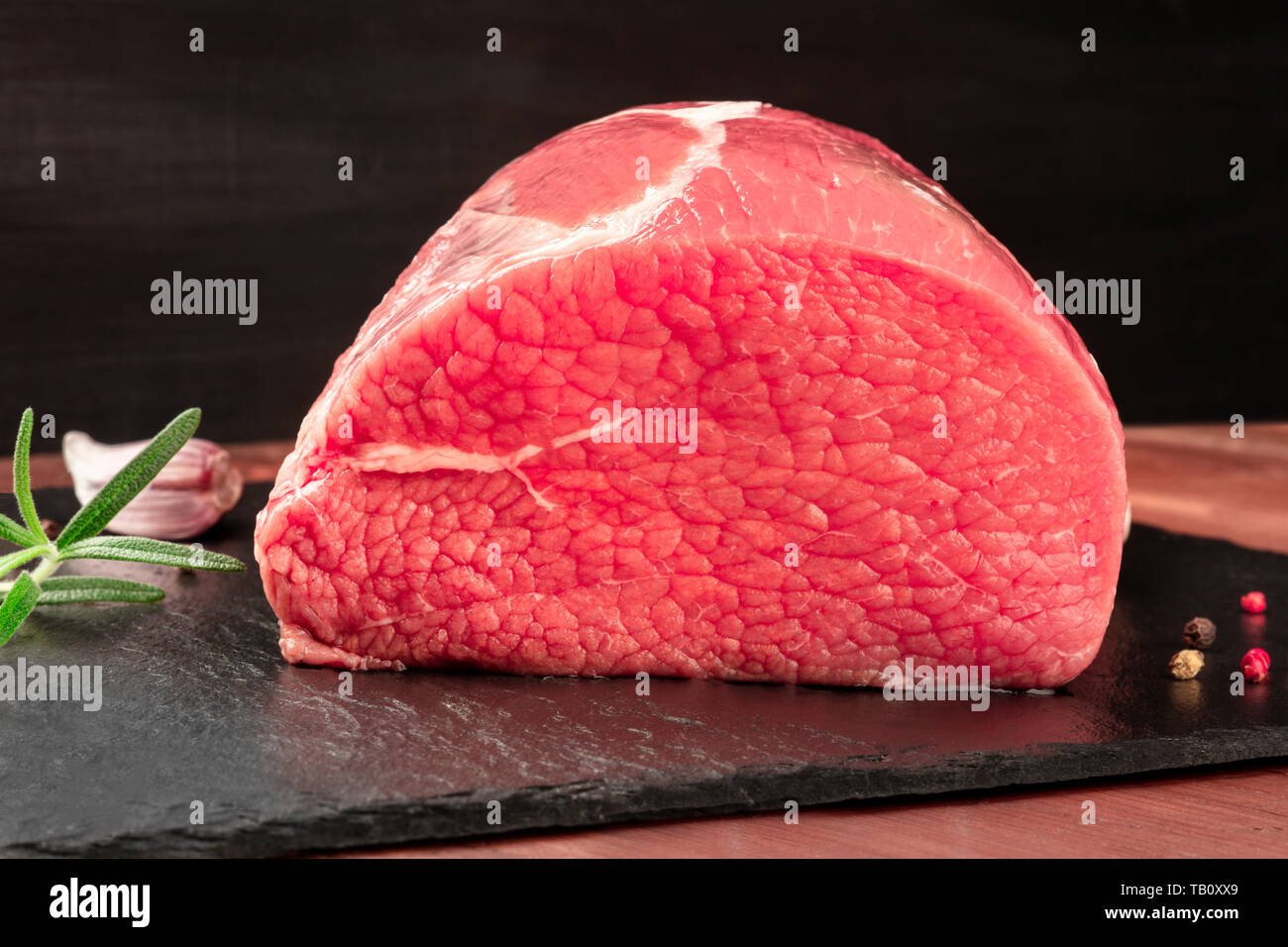 Eye round beef, a raw cut, with rosemary, garlic, and peppercorns, on a ...