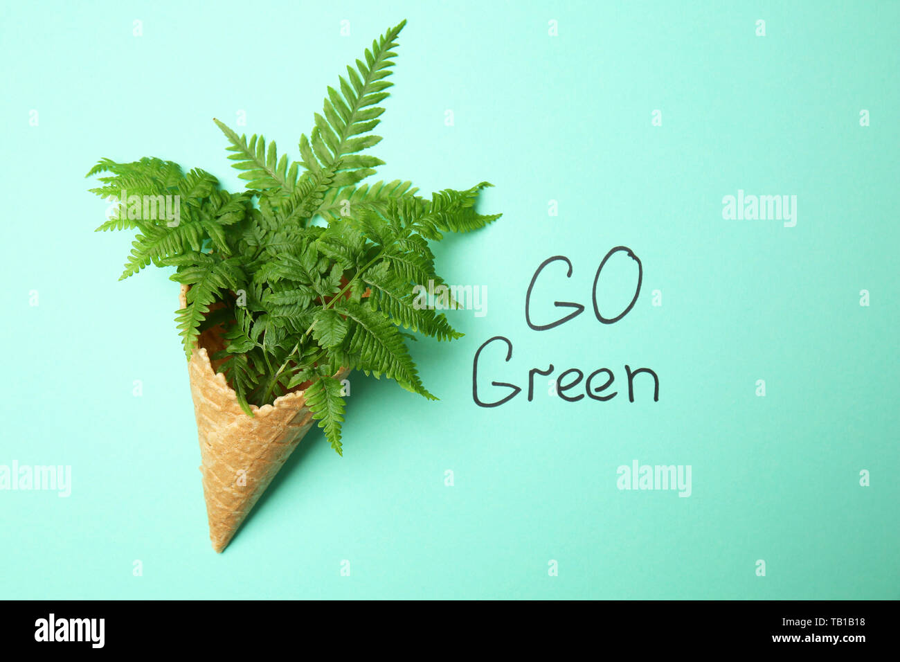Wafer cone with green fern leaves and text GO GREEN on color background ...