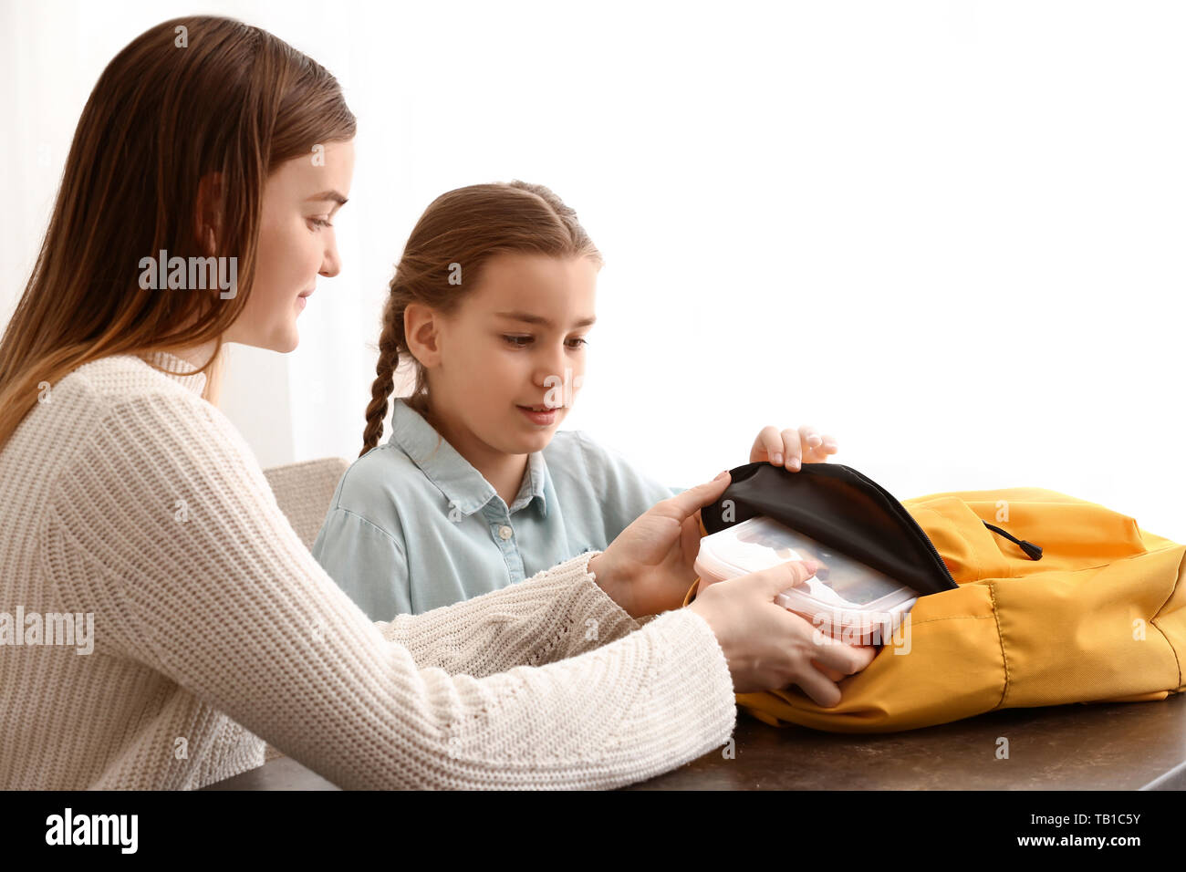 Mother putting lunch box into backpack of her little daughter before ...