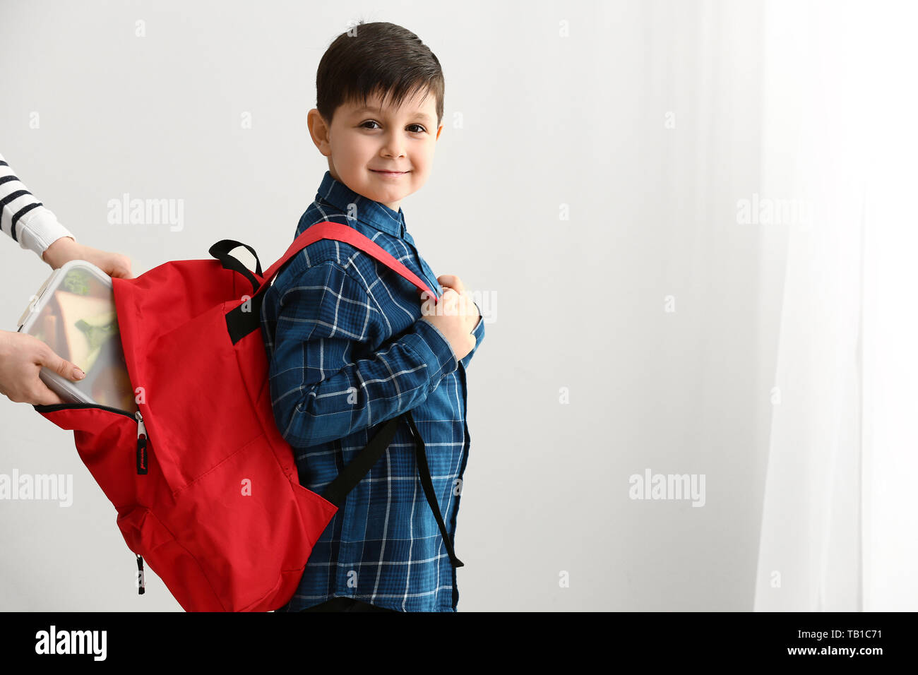 Mother putting lunch box into backpack of her little son before school ...