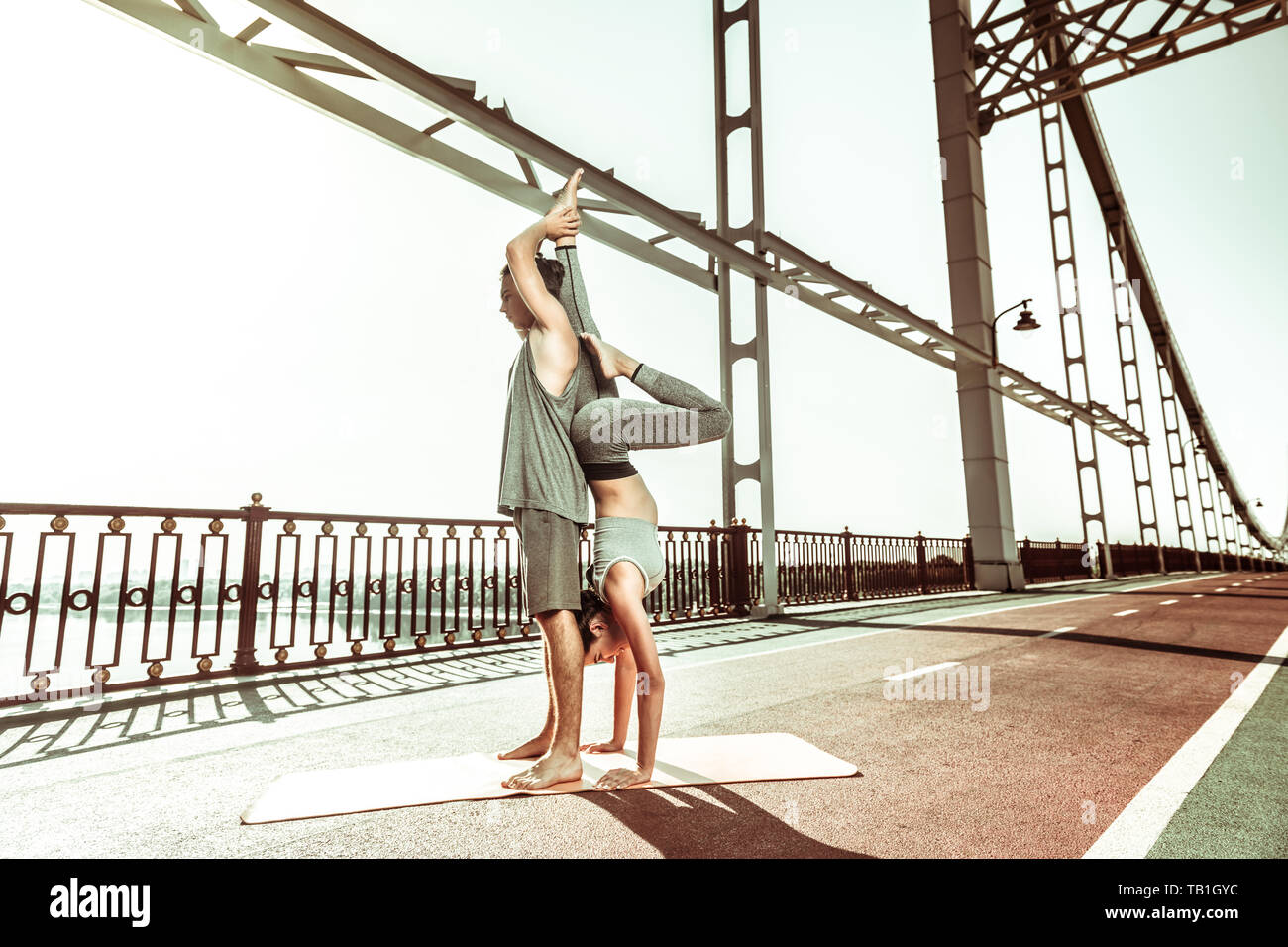 Slim woman practicing a candle stick asana assisted by her yoga partner ...