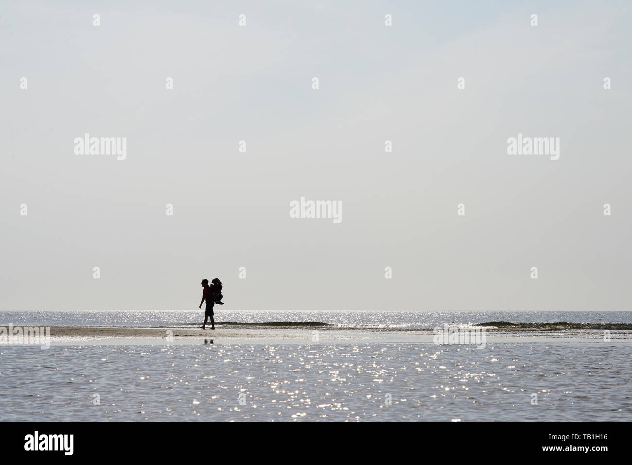 Amazing silhouette of a male backpackers walking across the shallow ...
