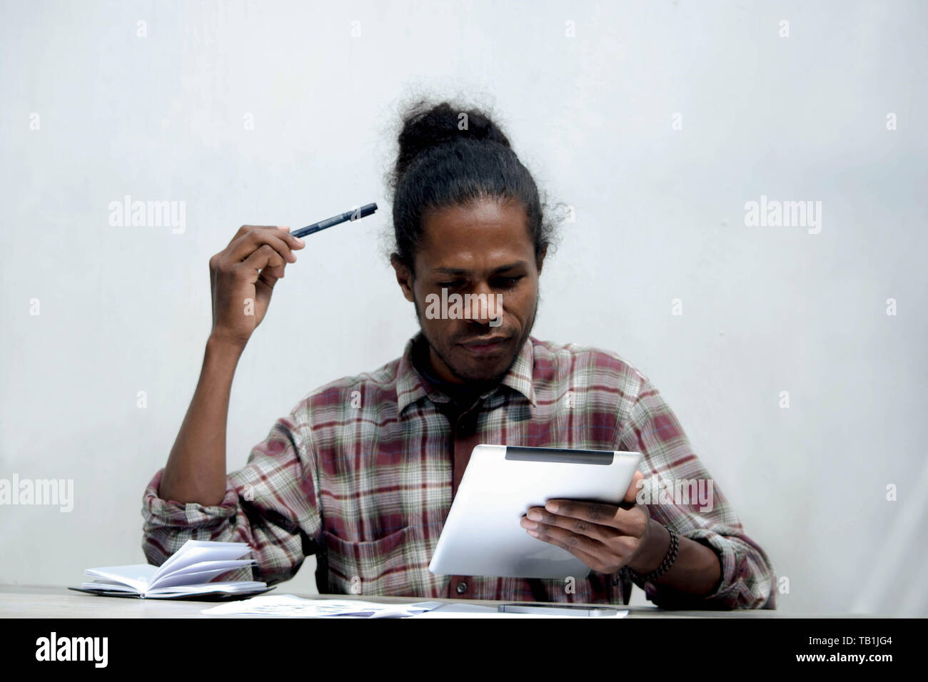 a young black man working and studying holding laptop and pen doing ...