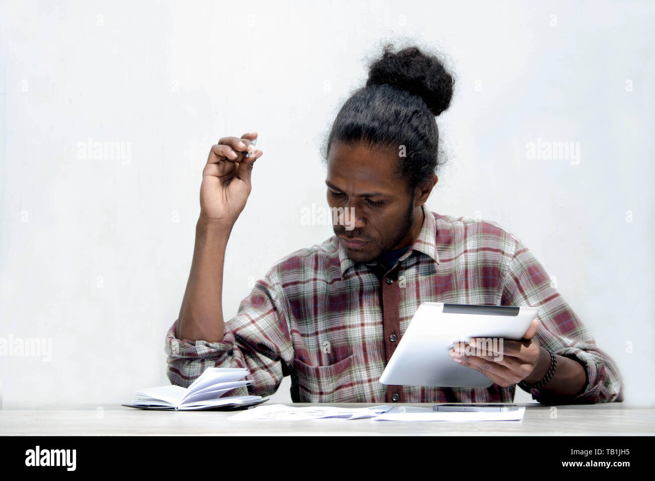 a young black man working and studying holding laptop and pen doing ...