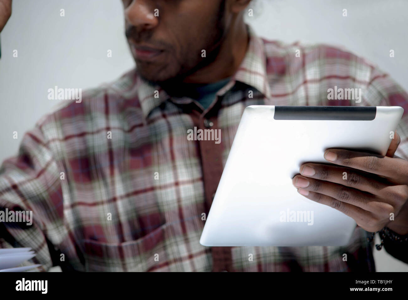 a young black man working and studying holding laptop and pen doing ...