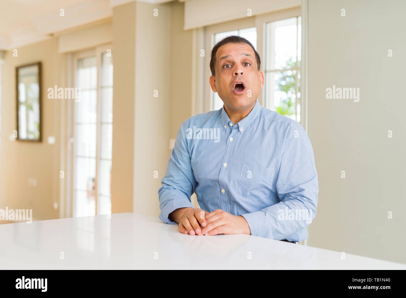 Middle age man sitting at home afraid and shocked with surprise ...
