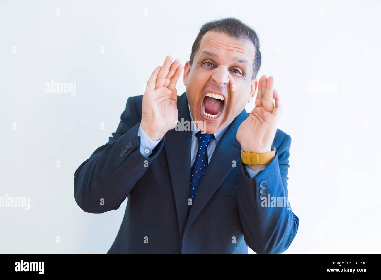 Middle age man shouting crazy with hands over mouth over white wall ...