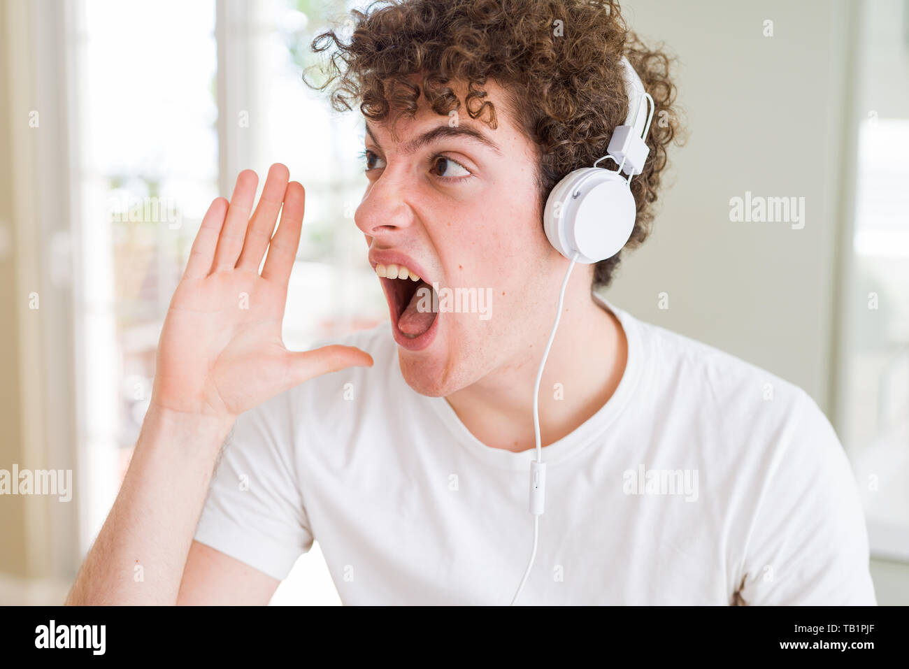 Young man listening to music wearing headphones at homes shouting and ...