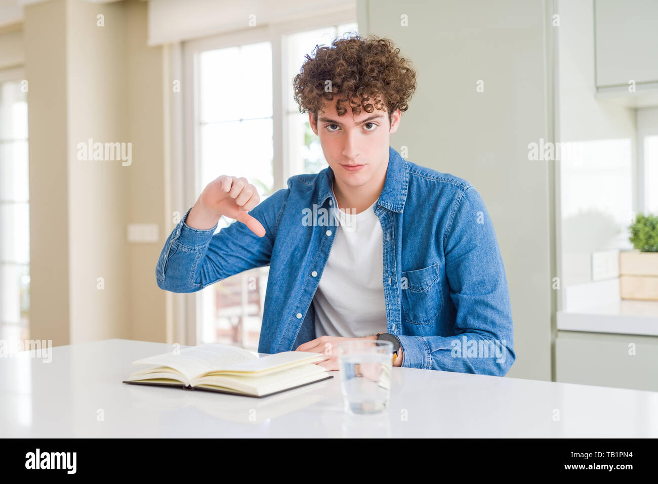 Young man reading a book at home with angry face, negative sign showing ...