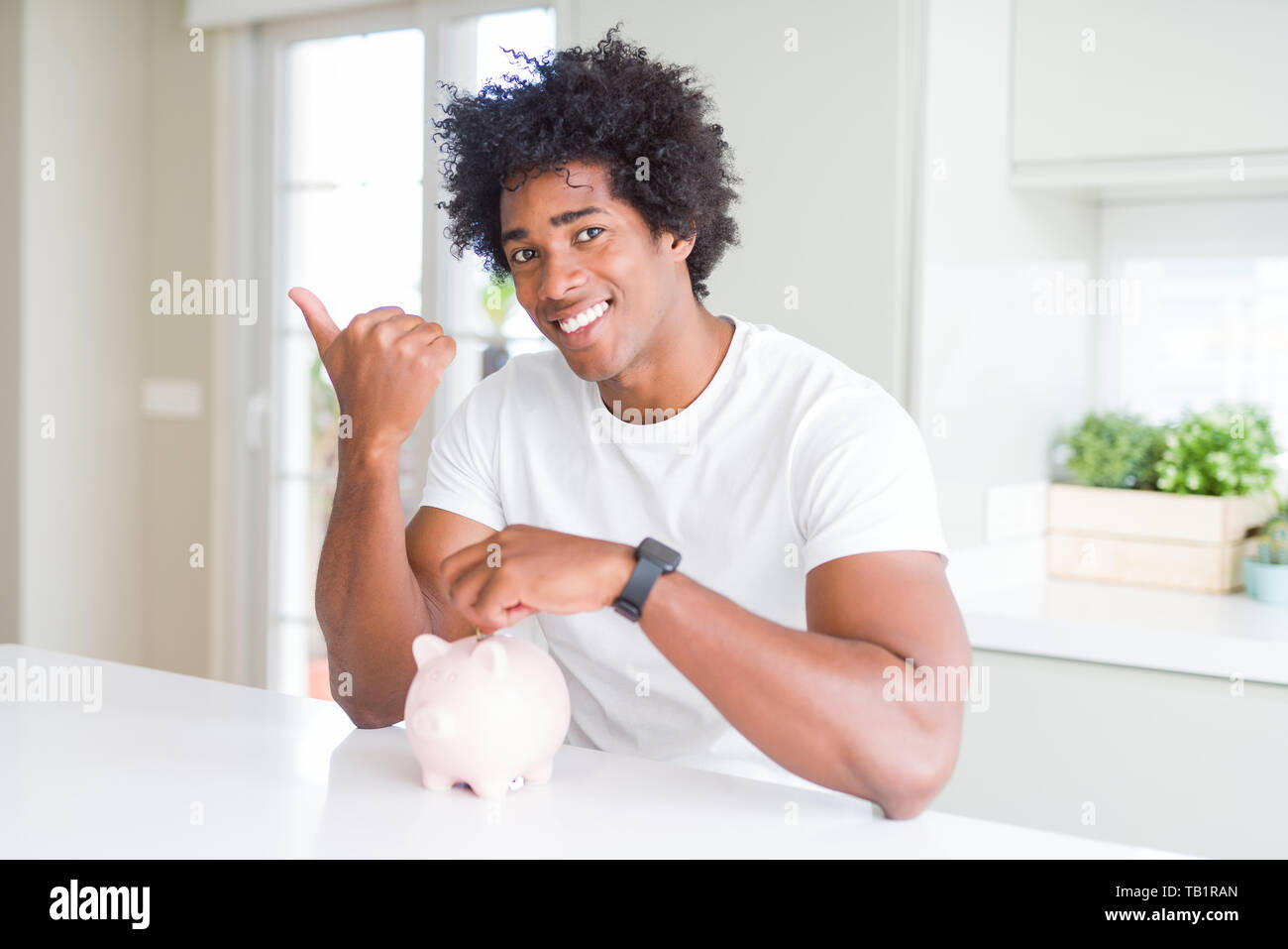 African American man putting a coin inside piggy bank pointing and ...