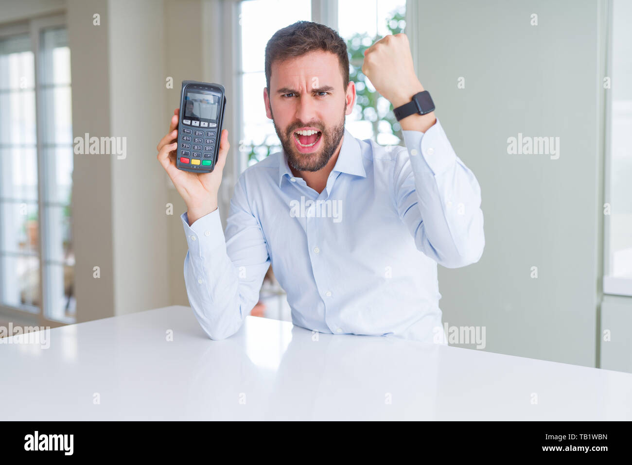 Handsome young man holding point of sale terminal annoyed and ...
