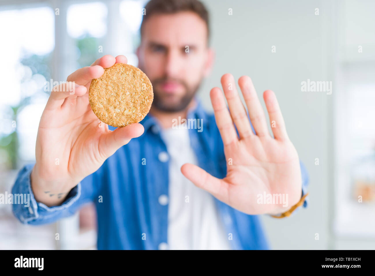Handsome man eating healthy whole grain biscuit with open hand doing ...