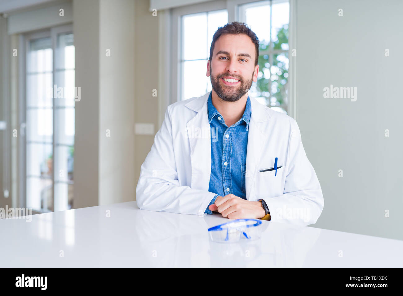 Handsome scientist man wearing white robe and safety glasses with a ...