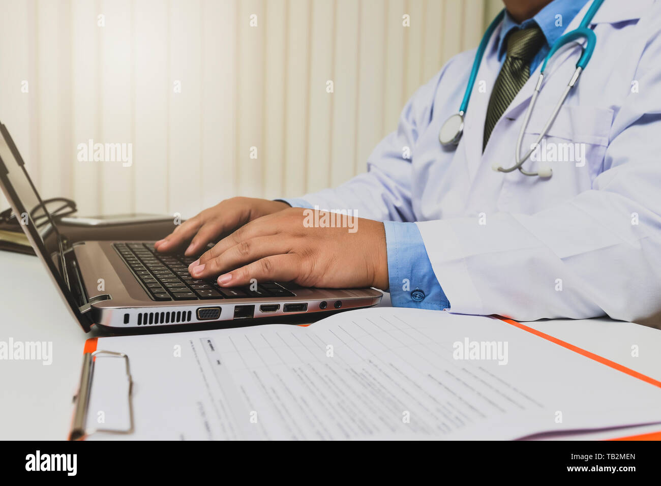doctor sitting at the table near the window in hospital and typing at ...