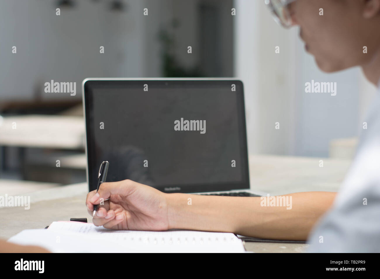 rear view student doing homework with laptop and writing in notebook at ...