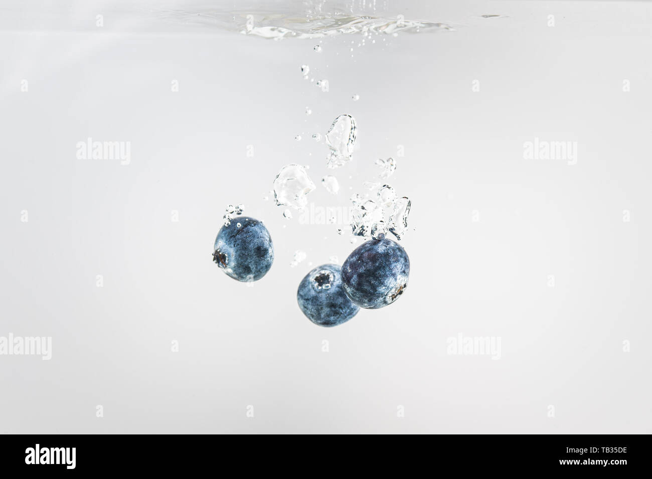Three Organic Blueberries sinking into water with air bubbles white ...