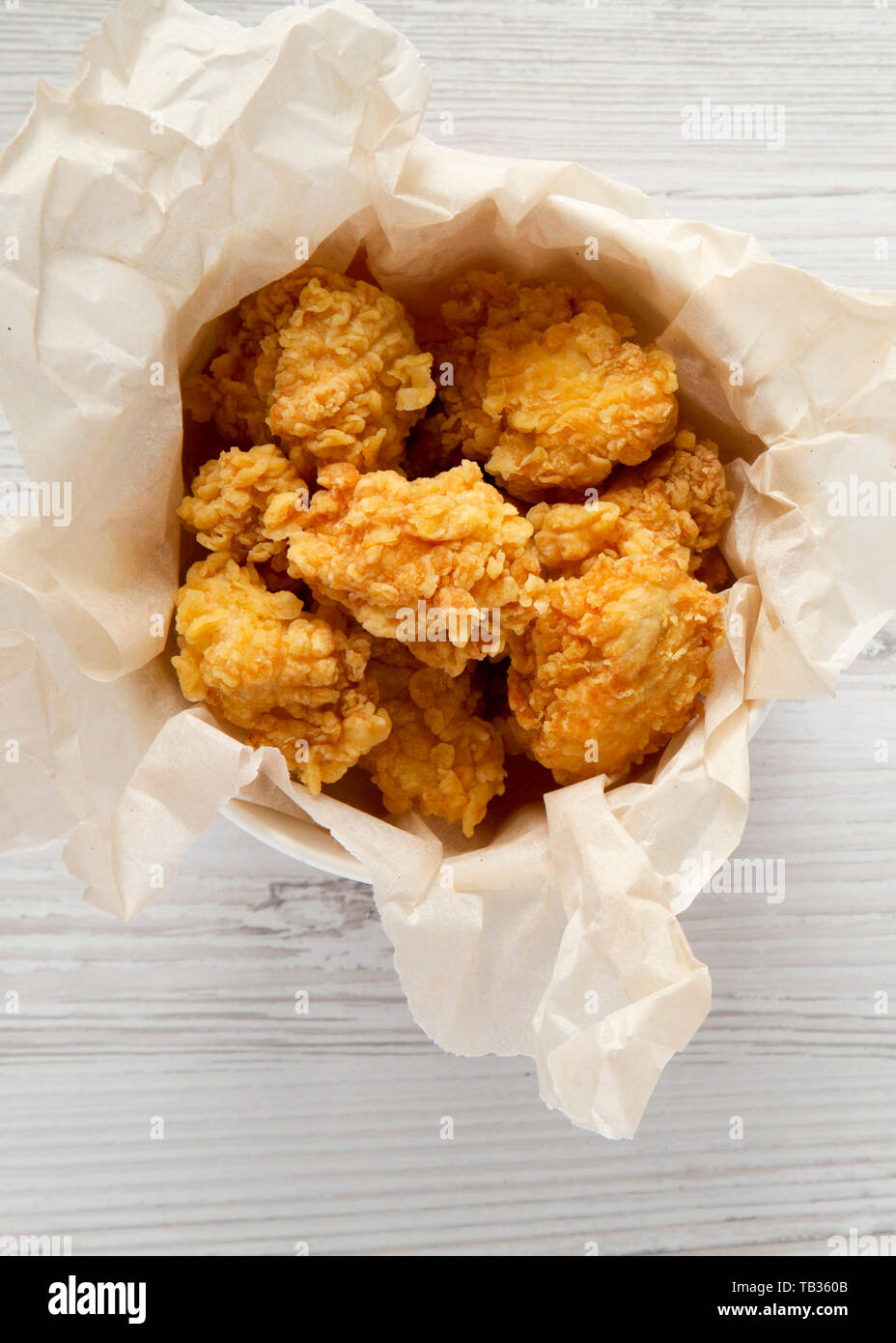 Fried chicken bites in a paper box over white wooden surface, top view ...