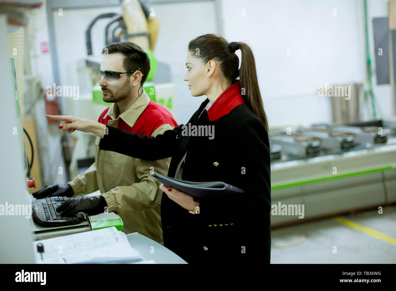 Pretty young woman controlling process in the factory with male worker ...