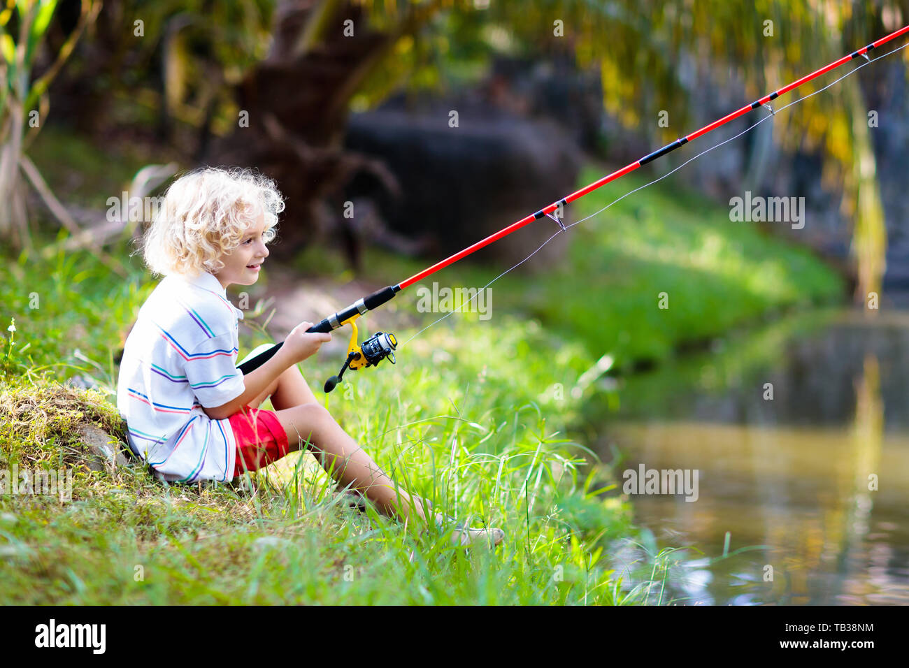 Boy fishing. Child with red rod catching fish in river on sunny summer ...