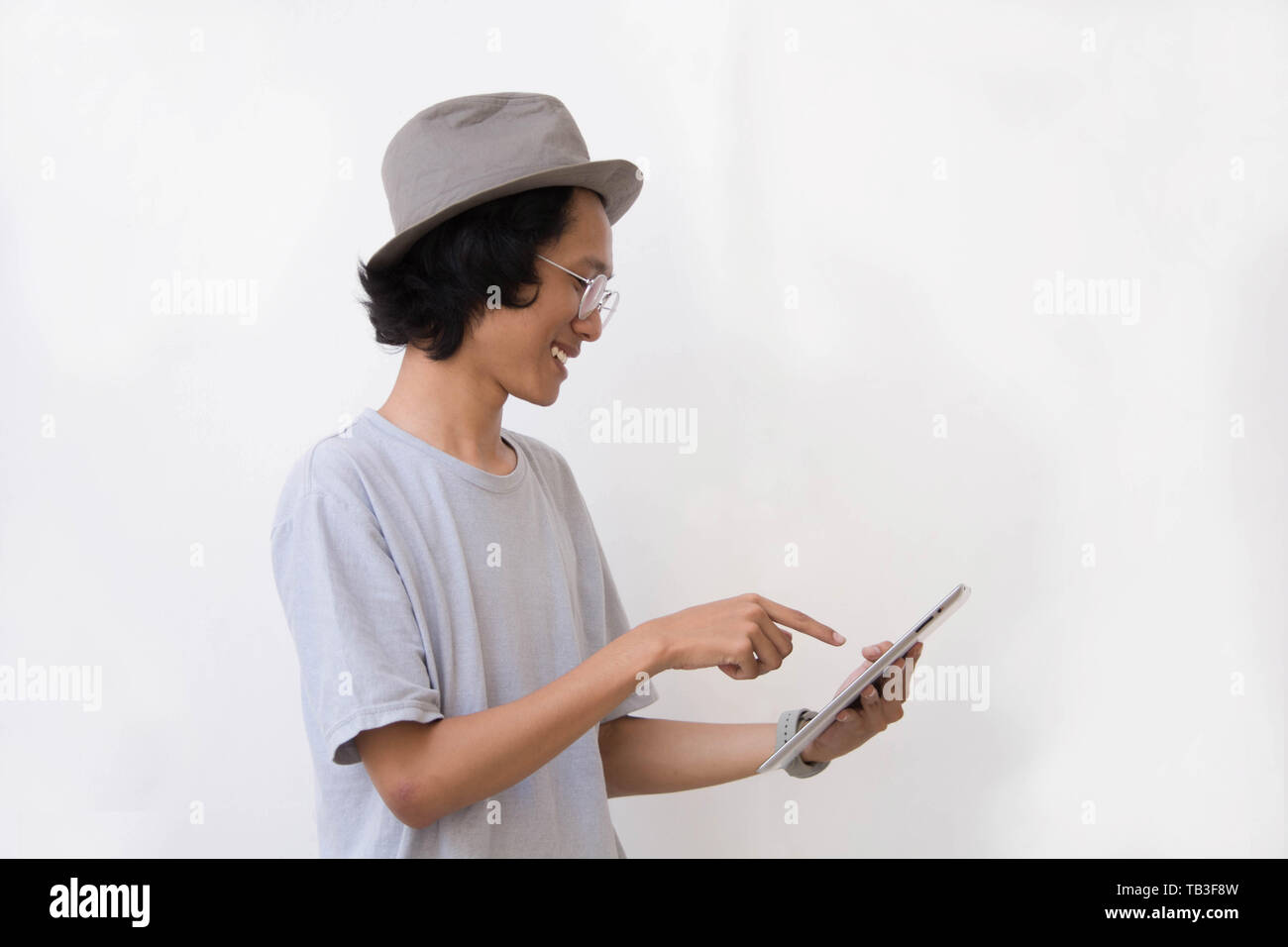 young asian man with fedora hat and glasses using tablet and smiling ...