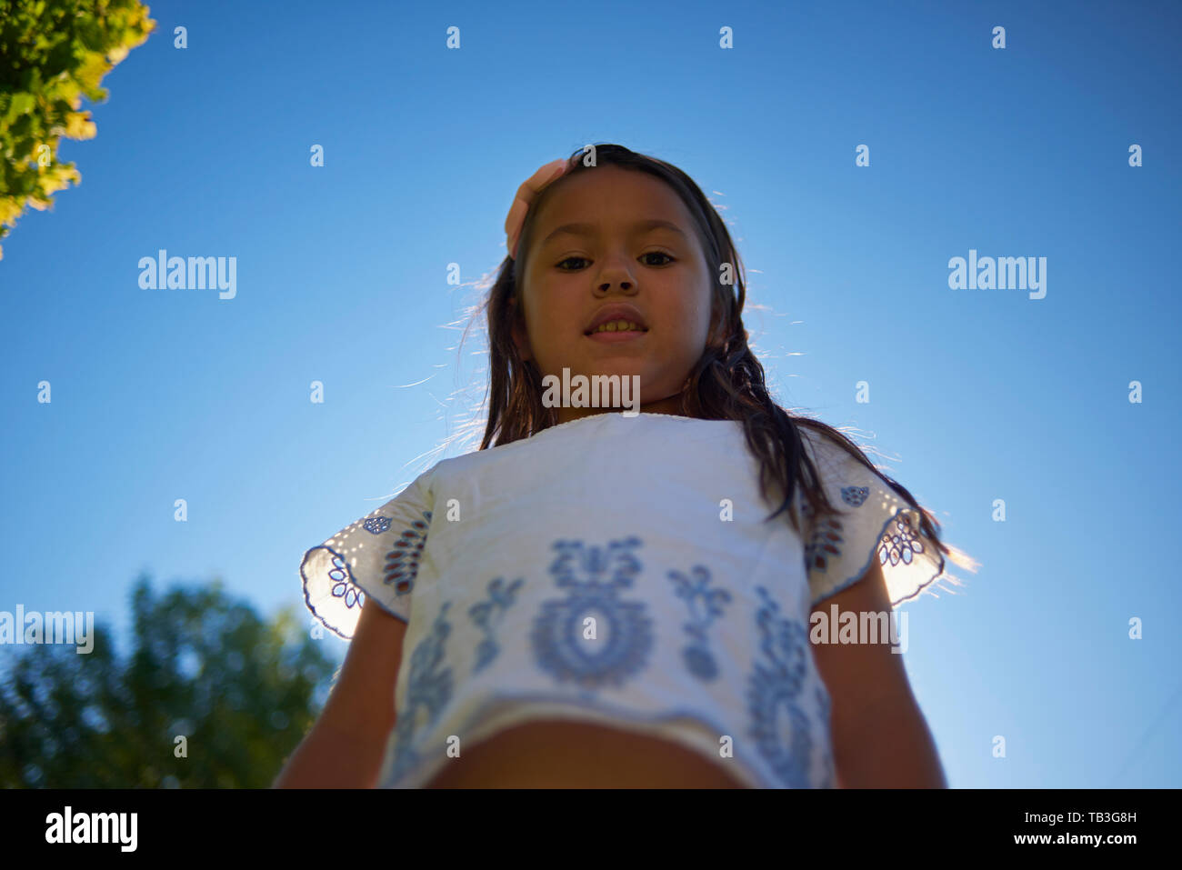 Low Angle Portrait Of A Beautiful Young Asian Girl In A White Dress In Summer Sunshine With Blue