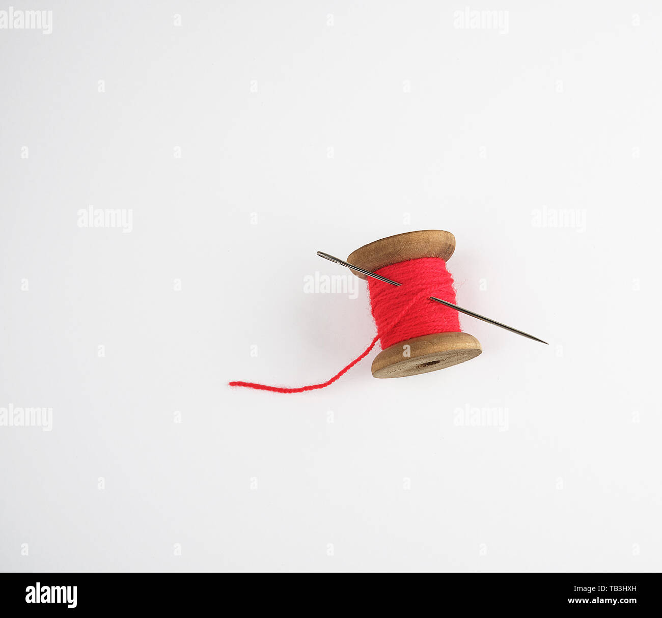wooden reel with red wool thread and a large needle, white background ...